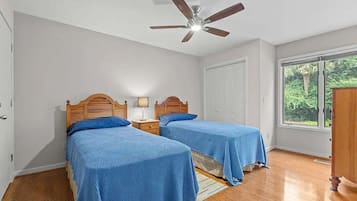 Quarto com duas camas, ventilador de teto, janela com vista para vegetação e uma porta.