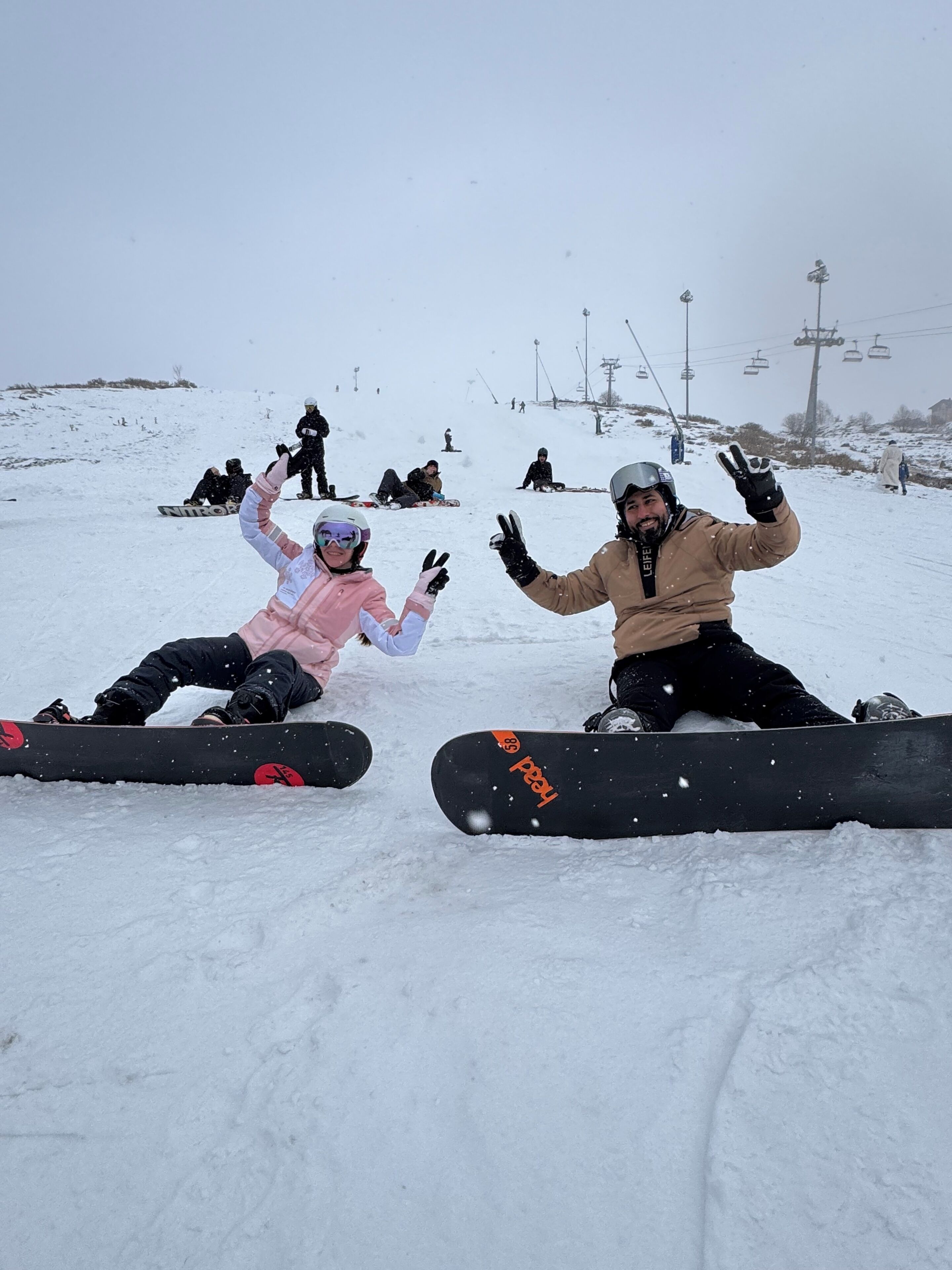 Uma área externa nevada com pessoas sentadas e praticando snowboard.