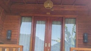 Um edifício de madeira com varanda, duas portas com painéis de vidro e duas pequenas mesas.