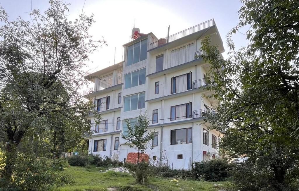 Um edifício residencial de vários andares com varandas, cercado por árvores e vegetação.