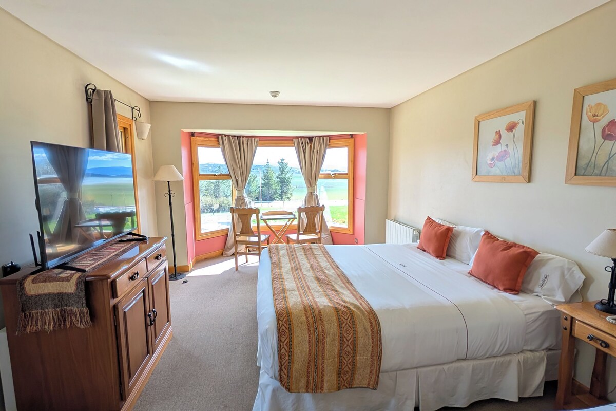 Quarto de hotel com uma cama grande, TV, escrivaninha e vista para o exterior.