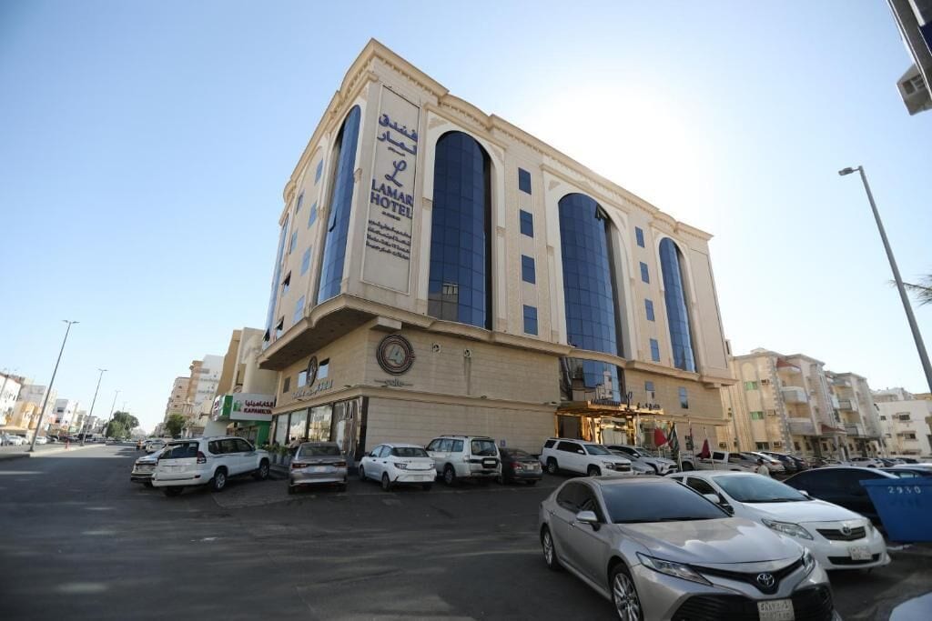 Um hotel com uma placa grande, vários andares e um estacionamento com vários carros.
