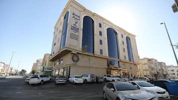Um hotel com uma placa grande, vários andares e um estacionamento com vários carros.