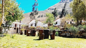 Paisagem rural com muro de pedra, mobiliário de madeira e montanha ao fundo.
