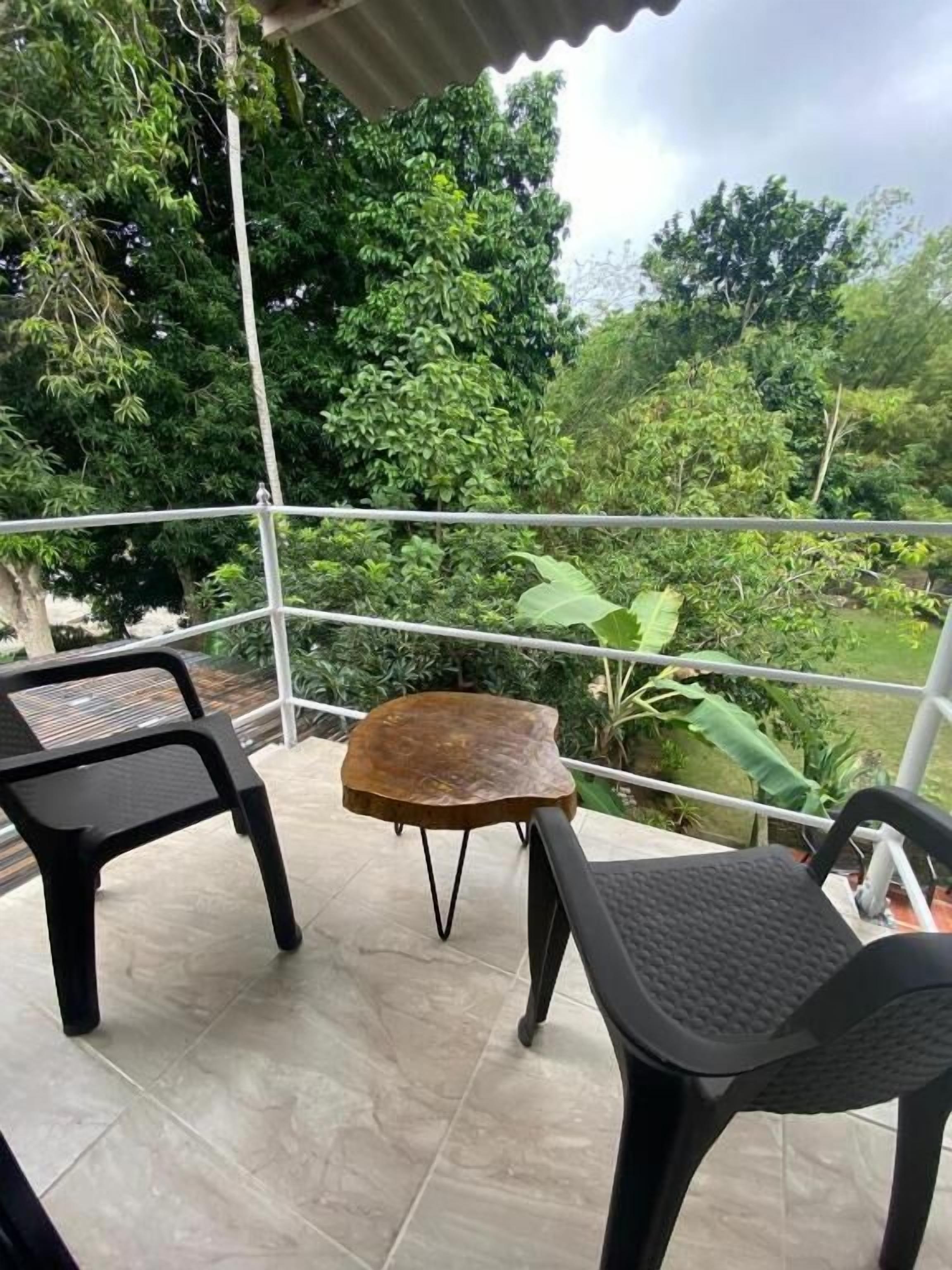 Varanda com duas cadeiras e uma mesa pequena, com vista para um jardim exuberante.
