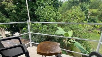 Varanda com duas cadeiras e uma mesa pequena, com vista para um jardim exuberante.
