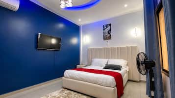 Quarto moderno com cama, televisão de tela plana, ventilador de teto e um detalhe decorativo na parede.