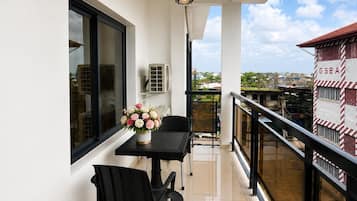 Uma varanda com mesa e cadeiras, um vaso de flores e vista para a paisagem urbana.