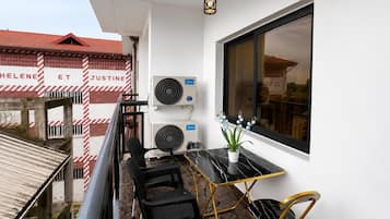 Uma varanda com duas unidades de ar condicionado, uma mesa com cadeiras e uma janela com vista para edifícios.