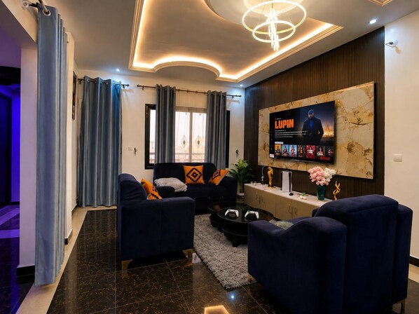 Uma sala de estar moderna com televisão de tela plana, sofás escuros, uma mesa de centro e um objeto decorativo na parede.