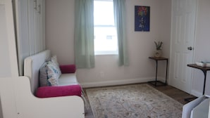 Quarto com sofá branco, tapete estampado, mesa pequena e uma porta.