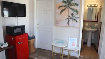 Quarto com televisão de tela plana na parede, um aparelho vermelho, uma moldura com imagem e uma mesa pequena com um objeto de vidro.