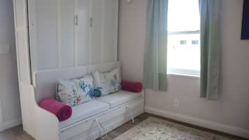 Quarto com sofá branco, tapete estampado e janela com cortinas verde-claras.