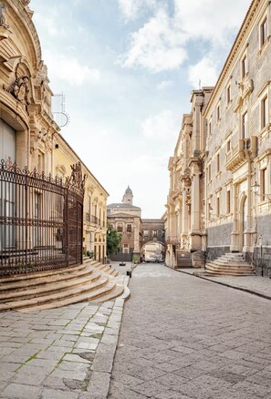 Ruas de calçada ladeadas por edifícios históricos com fachadas ornamentadas e um arco central que dá acesso a uma estrutura em cúpula.
