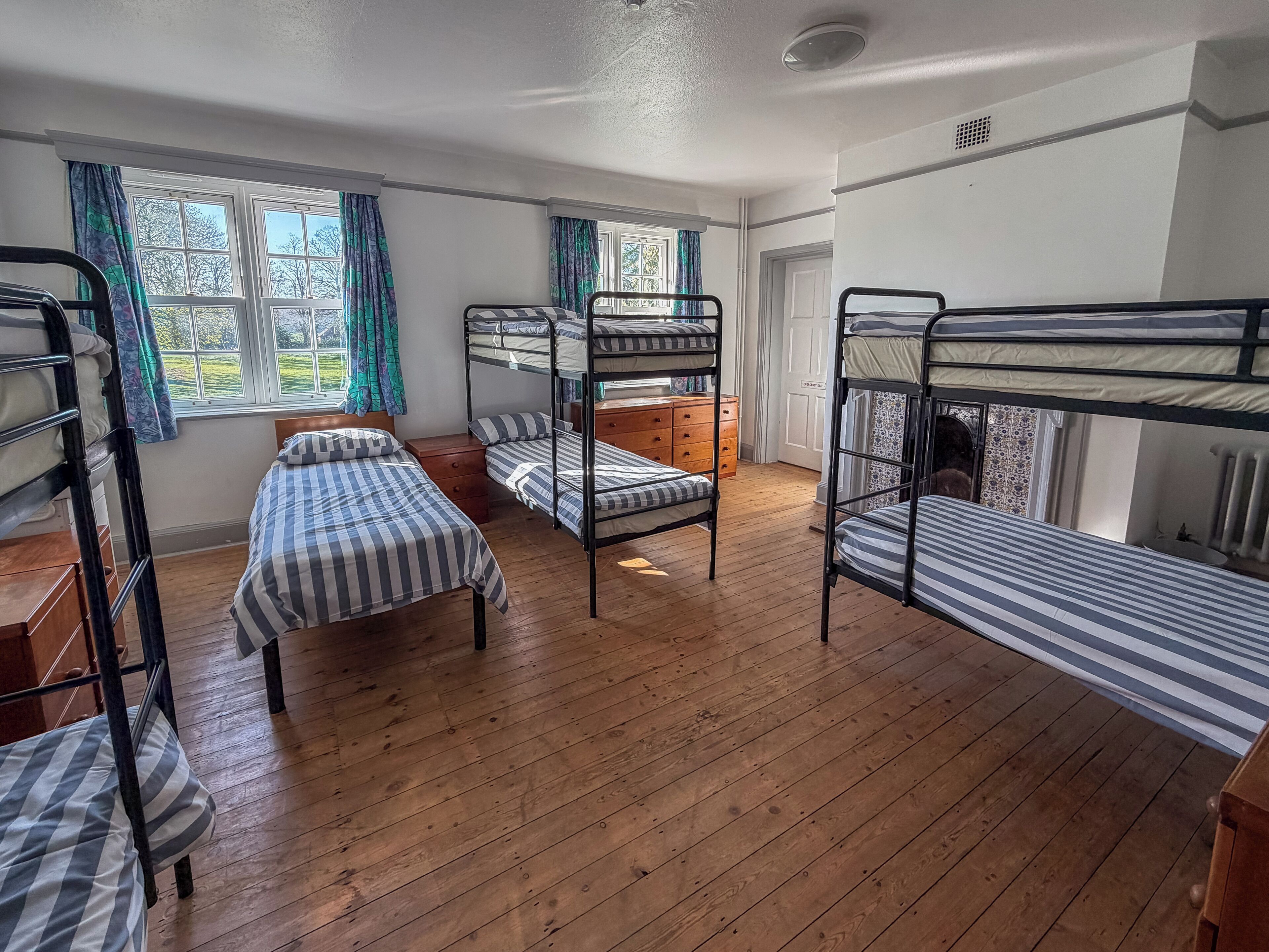 Quarto com beliches, piso de madeira e janela com cortinas.