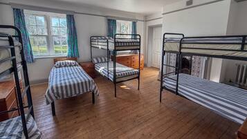 Quarto com beliches, piso de madeira e janela com cortinas.