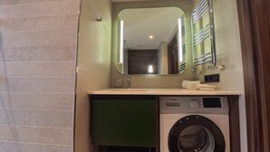 Casa de banho de hotel com lavatório, espelho, toalha e máquina de lavar roupa.