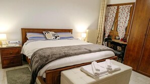 Quarto com cama, mesas de cabeceira, cômoda, um banco e espelho.