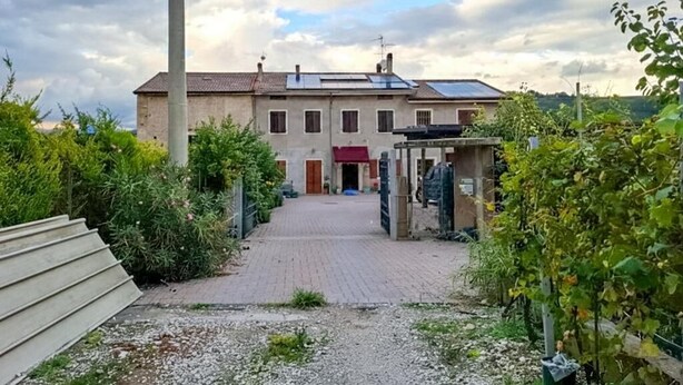 Um edifício com entrada pavimentada, uma pequena área coberta e um jardim com diversas plantas.