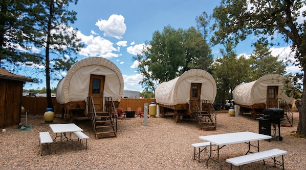 Um camping com carroças cobertas, mesas de piquenique e churrasqueira.