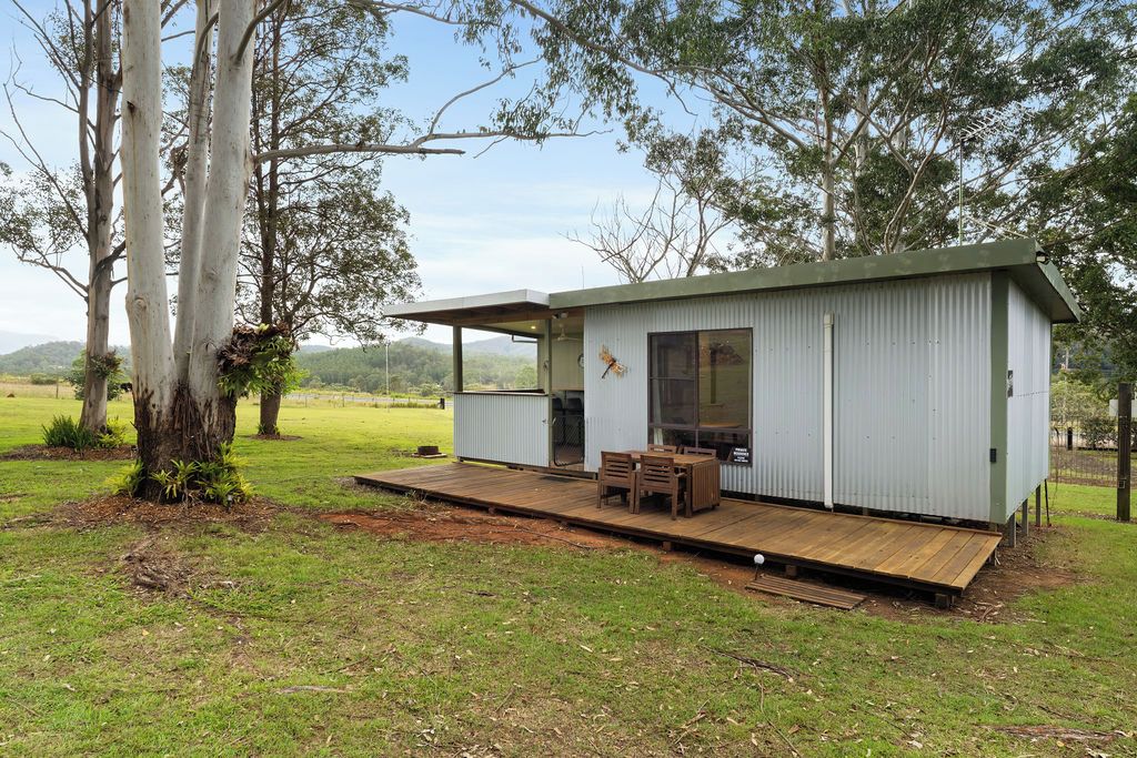 Estrutura metálica térrea com deck e área externa para sentar, cercada por árvores e um campo gramado.