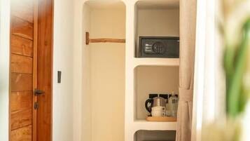 Um corredor com porta de madeira, prateleira com vasos decorativos, máquina de café e um pequeno frigorífico.