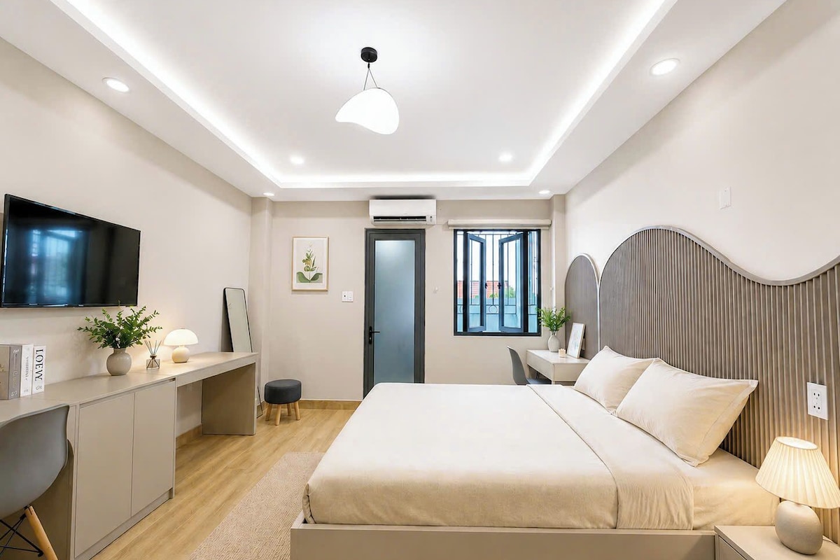 Quarto moderno com cama, mesa de cabeceira, escrivaninha e televisão.