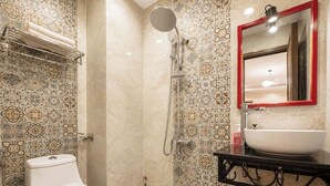 Um banheiro com vaso sanitário, chuveiro com chuveiro manual, pia com espelho e azulejos estampados nas paredes e no chão.