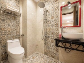 Um banheiro com vaso sanitário, chuveiro com chuveiro manual, pia com espelho e azulejos estampados nas paredes e no chão.