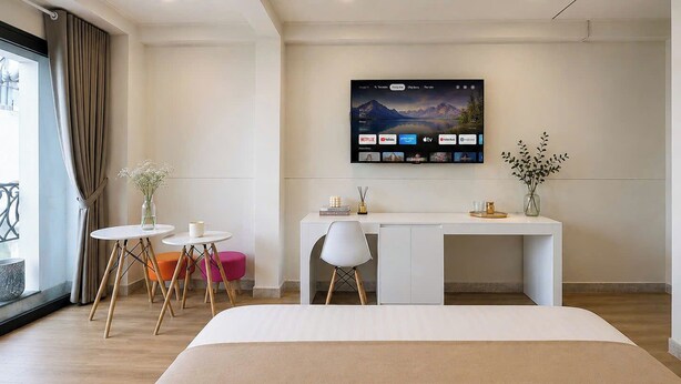 Quarto de hotel moderno com cama, escrivaninha, televisão e janela com cortinas.
