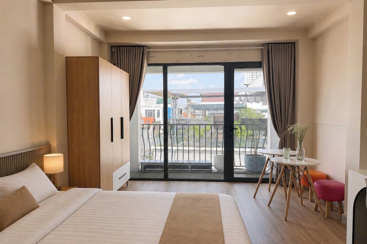 Quarto de hotel com cama, escrivaninha, cadeira, mesa e varanda com vista para edifícios.