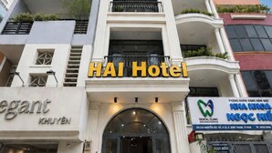 Entrada de hotel com uma placa indicando 'HAI Hotel' e uma clínica dentária do outro lado da rua.