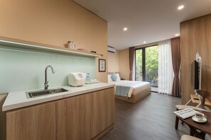 Quarto de hotel com cozinha compacta, uma cama, área de refeições e uma janela grande com cortinas.