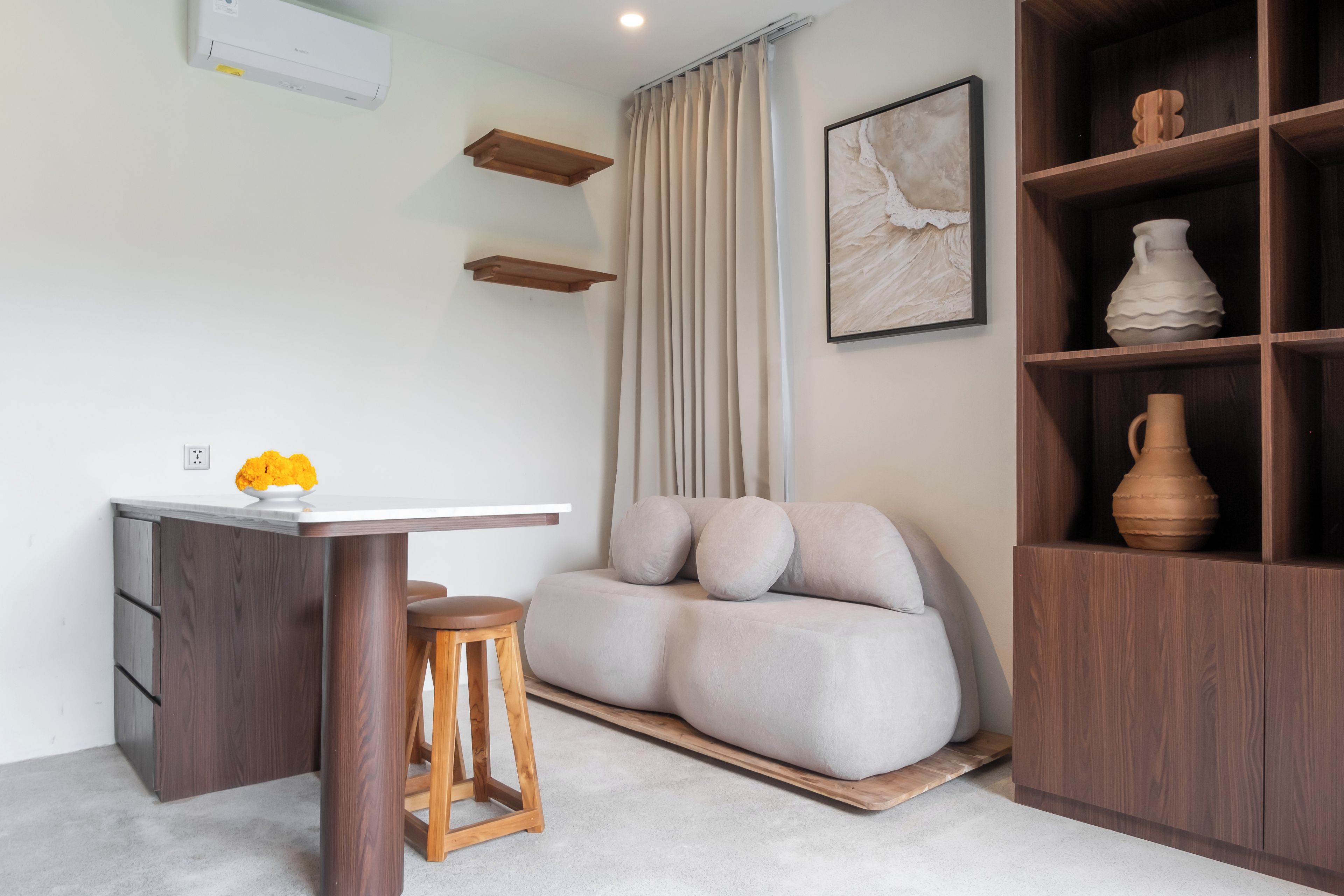 Um espaço de estar moderno com um sofá, uma mesinha, um banquinho, uma estante com objetos decorativos e um ar condicionado fixado na parede.