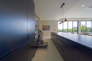 Cozinha moderna com uma ilha grande, eletrodomésticos de aço inoxidável e vista para o exterior.