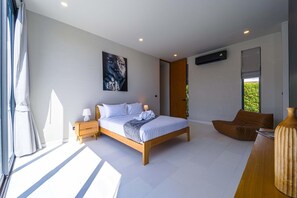 Quarto moderno com uma cama grande, uma mesinha de cabeceira com abajur, uma cadeira de madeira e uma janela ampla.