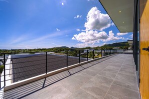 Varanda com vista para um parque de estacionamento e colinas ao longe, sob um céu limpo.