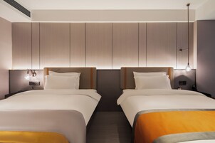 Quarto de hotel com duas camas, cabeceira com painel de luz, luminárias laterais e painel de controle na parede.
