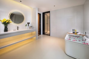 Casa de banho moderna com toucador, espelho grande, banheira com pétalas de rosa e porta que dá para outro quarto.