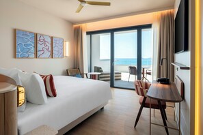 Quarto de hotel com cama, escrivaninha, cadeira, televisão e vista para o mar.