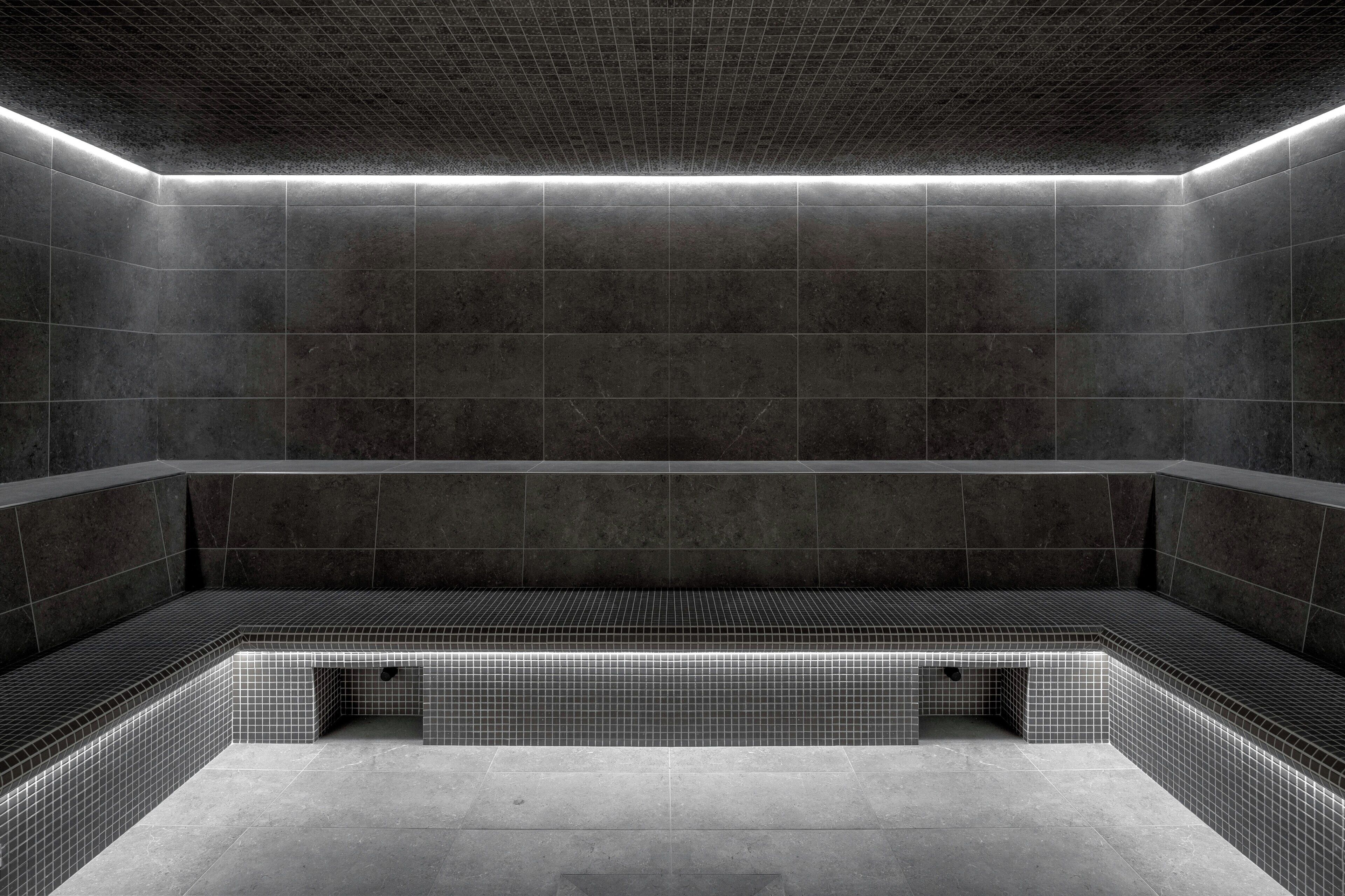 Piscina interior moderna, com iluminação suave, paredes revestidas de azulejos escuros e um banco ao longo da borda.
