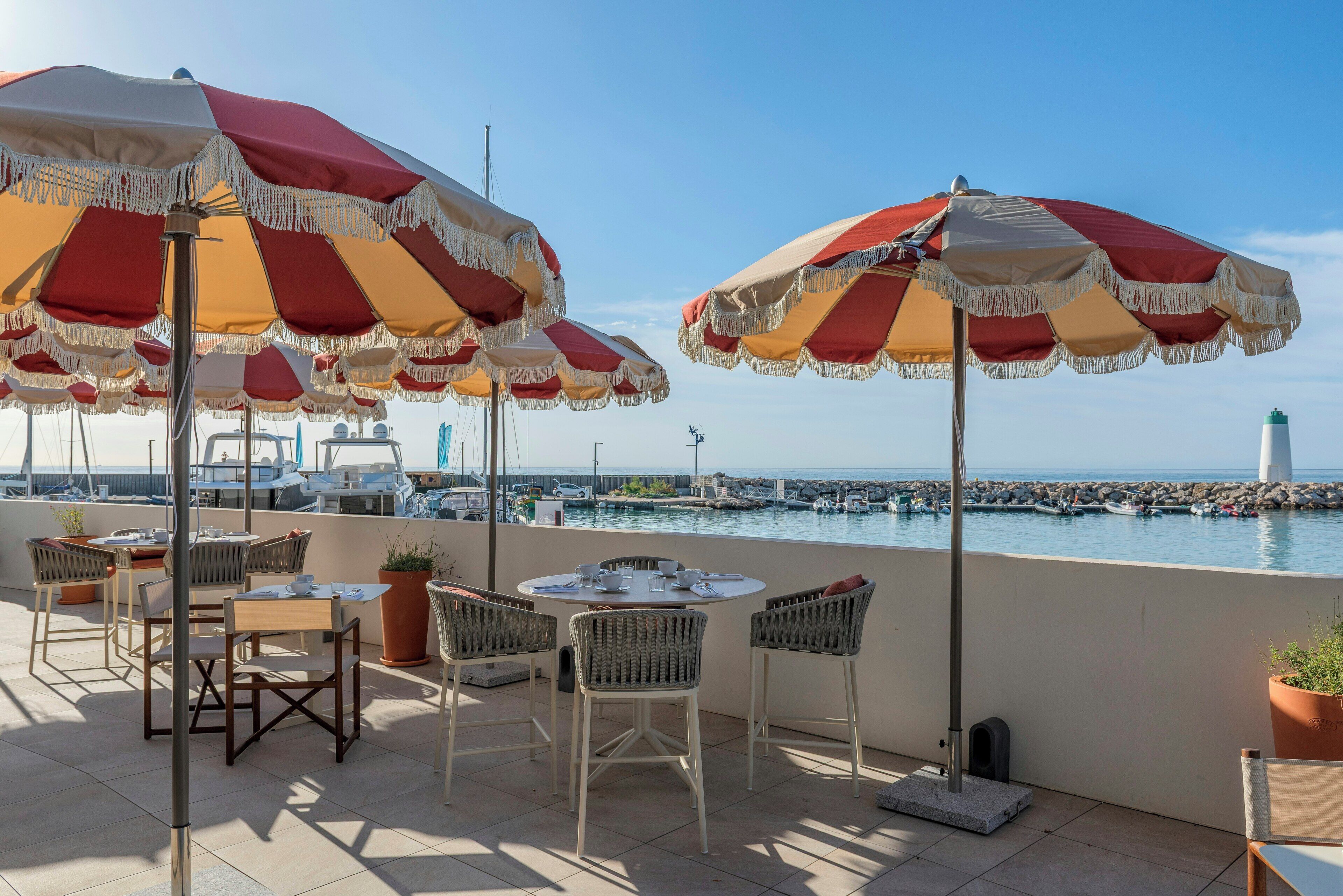 Terraço com área de estar ao ar livre, guarda-sóis e vista para o mar e barcos.