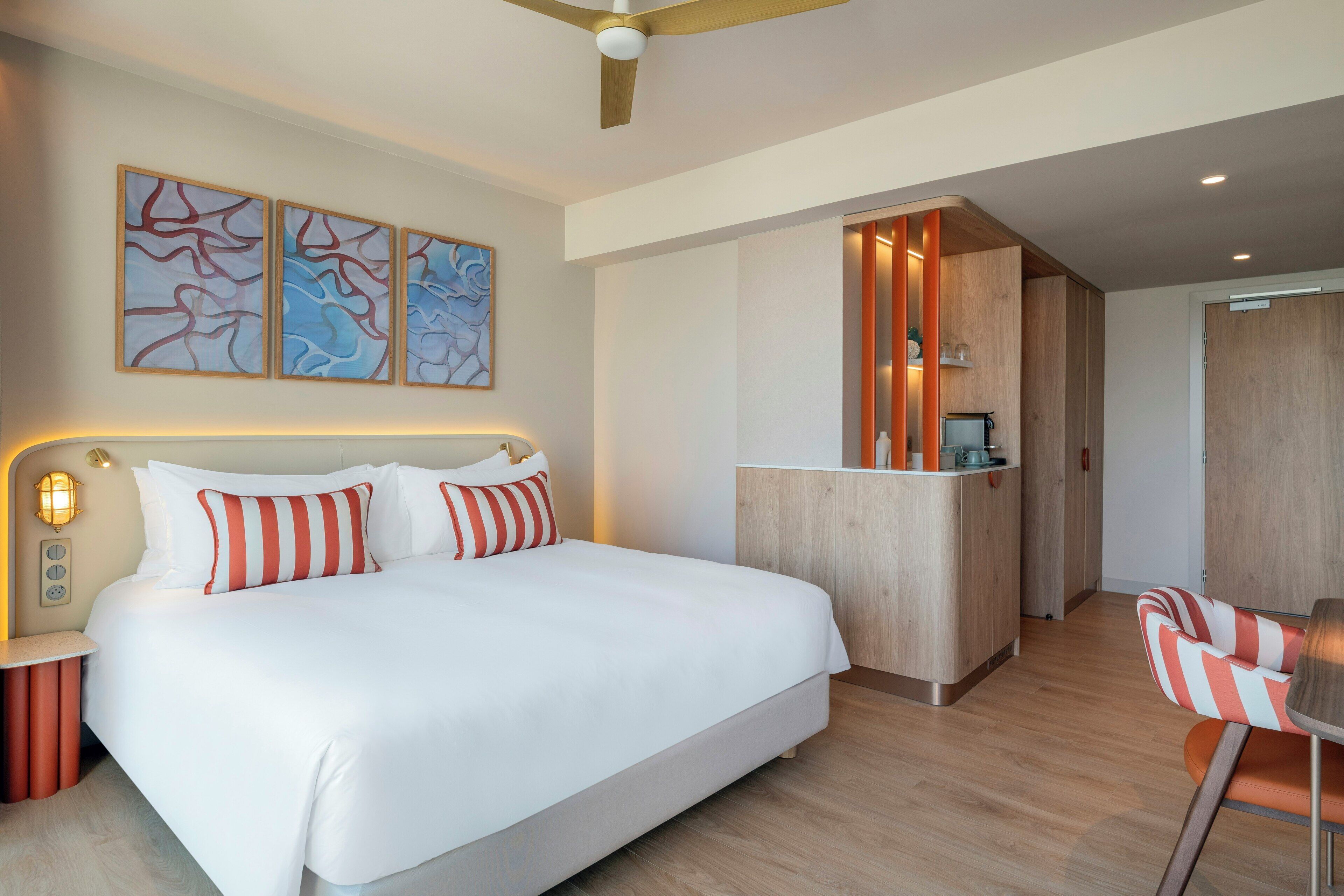 Quarto de hotel com uma cama grande, uma escrivaninha e uma cadeira. Há três obras de arte fixadas na parede acima da cama.