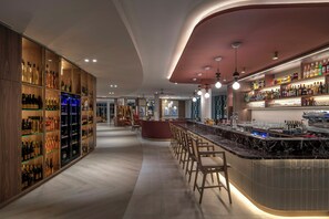 Uma área de bar com bancada de mármore, banquetas e prateleiras cheias de garrafas de bebidas.