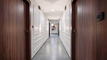 Corredor de hotel com portas de madeira, piso ladrilhado e luminária no teto.