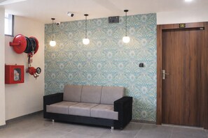 Quarto com parede estampada, sofá, porta com a etiqueta '101' e extintor de incêndio.