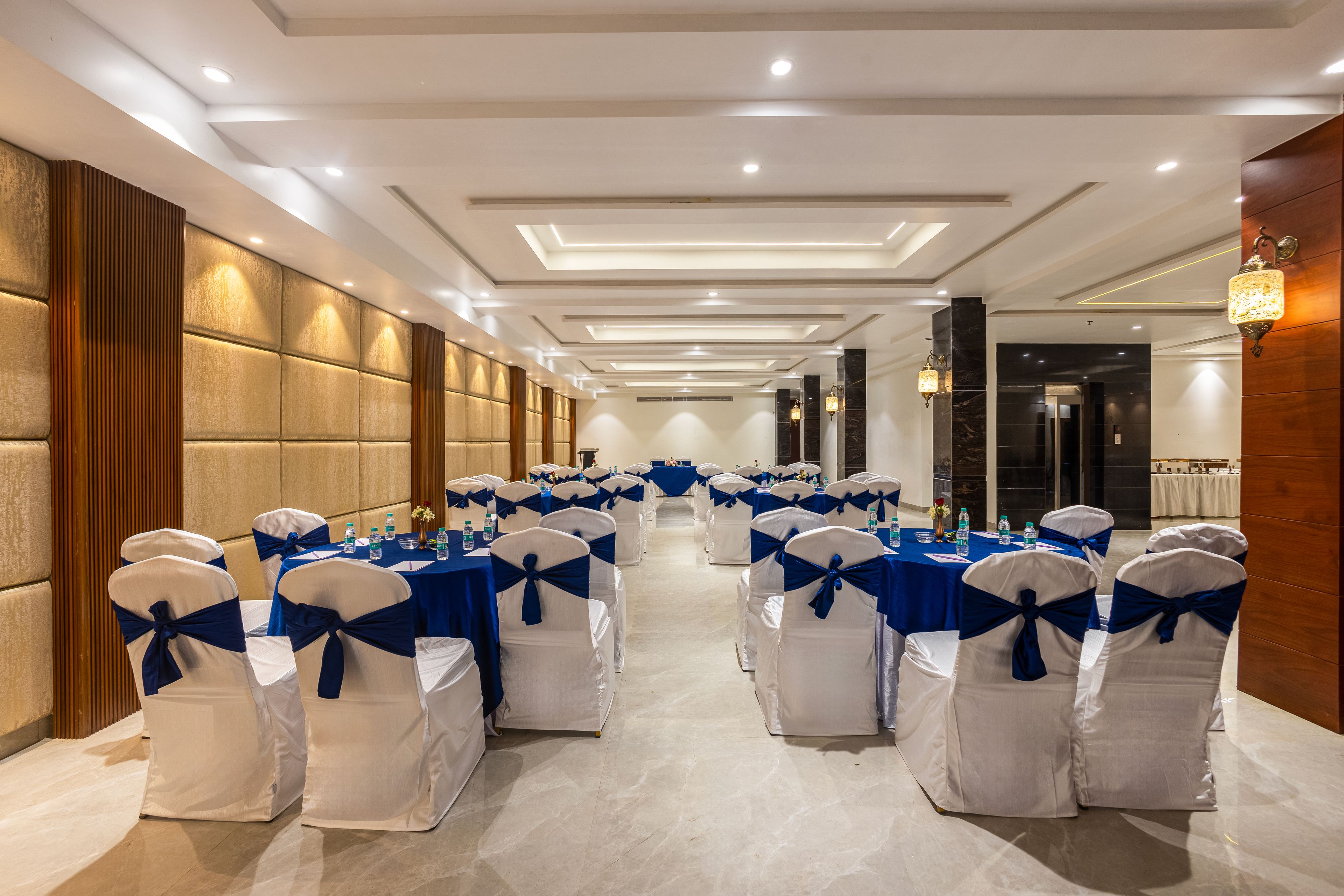 Sala de conferências com fileiras de mesas e cadeiras, equipada com garrafas de água e cartões de identificação.