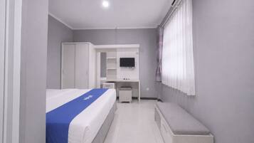 Quarto de hotel com cama, escrivaninha, cadeira, guarda-roupa, televisão e janela com cortinas.