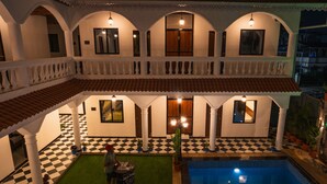 Hotel com piscina, piso xadrez e área externa coberta com colunas e corrimão.