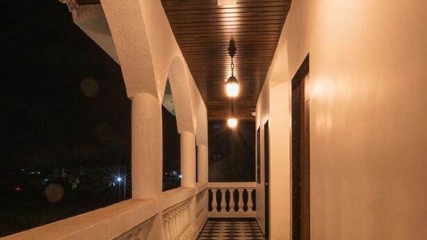 Um corredor com piso xadrez, paredes brancas e teto de madeira.